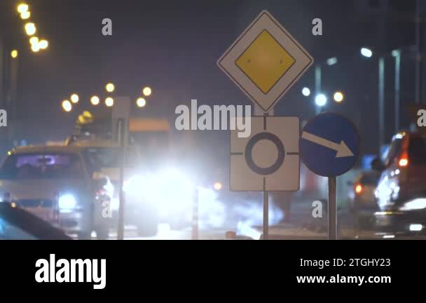 Roundabout road signs with blurred cars on city street traffic at night ...