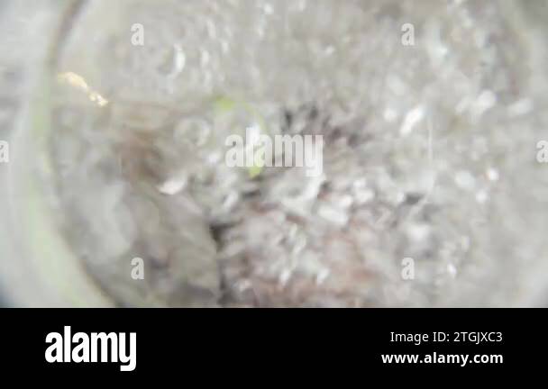 Camera in a glass, bottom view. A man with a beard pours and drinks ...