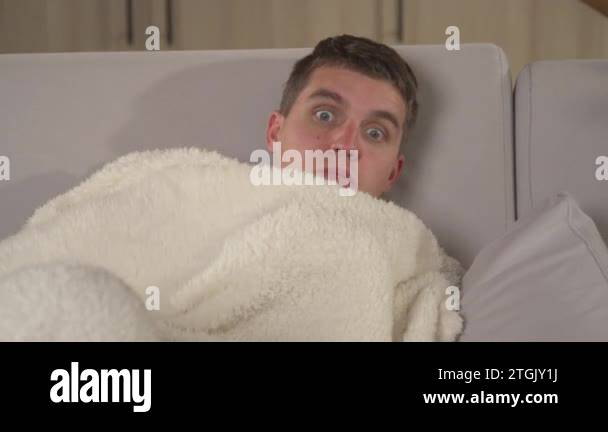 CLOSE UP Young guy being afraid while watching horror movie covered ...