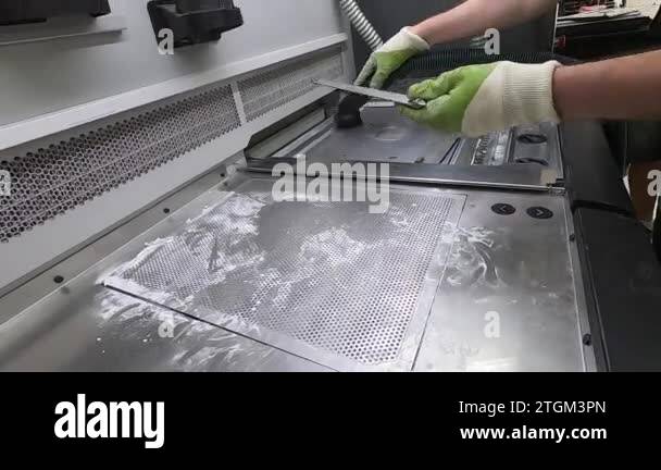 A male worker cleans the surface of an industrial 3D printer from white ...