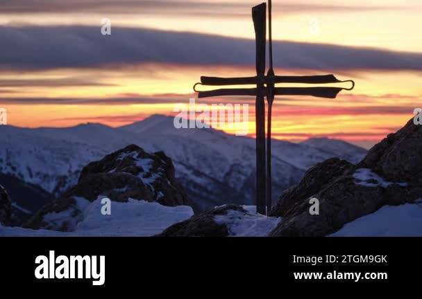 Pan shot of a Christian Catholic cross on top of a mountain in winter ...