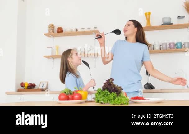 Happy mother dances and sings with her daughter in a modern kitchen ...