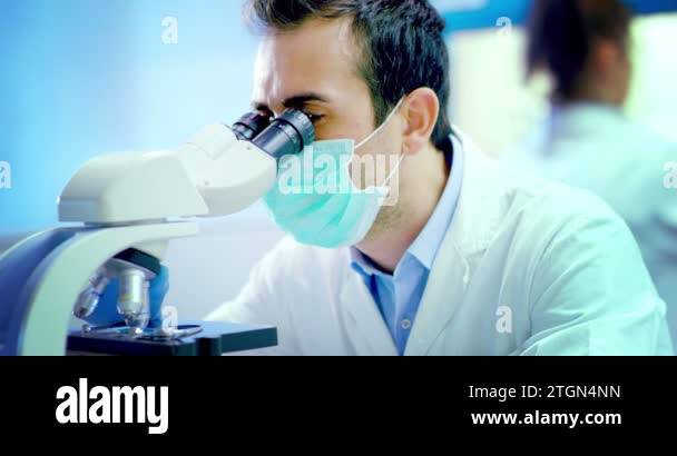 young and charming doctor look in microscope accomplishes some routine medical procedures and ...