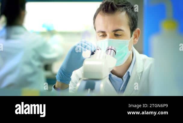 young and charming doctor look in microscope accomplishes some routine ...