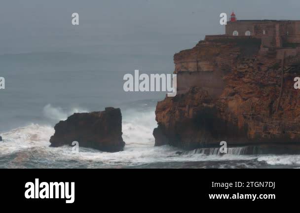 Massive ocean waves crashing the high cliffs with Farol de Nazare ...