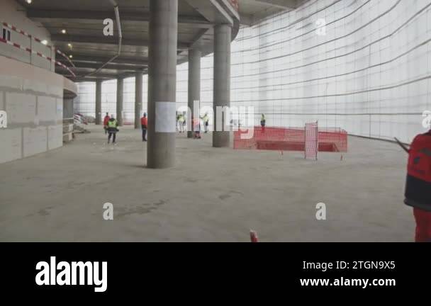 Builders in uniform walk along hall with columns at unfinished stadium ...