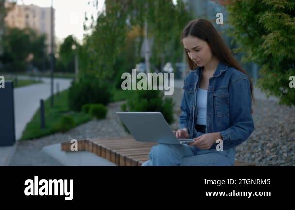 Caucasian woman sitting on the bench working on the laptop near the ...