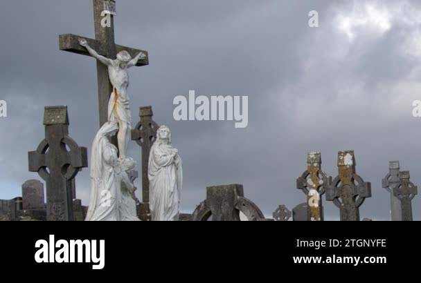 A large stone crucifixion of Jesus Christ in a Catholic cemetery in Ireland. Tombstones in the ...