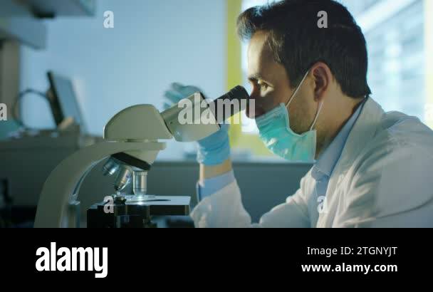 young and charming doctor look in microscope accomplishes some routine medical procedures and ...