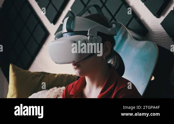 Young woman in a virtual reality helmet sitting on a sofa and communicating in the virtual world ...