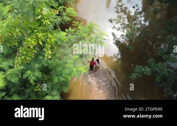 Lost woman with female child walking along overflowed road surrounded by forest trees during ...