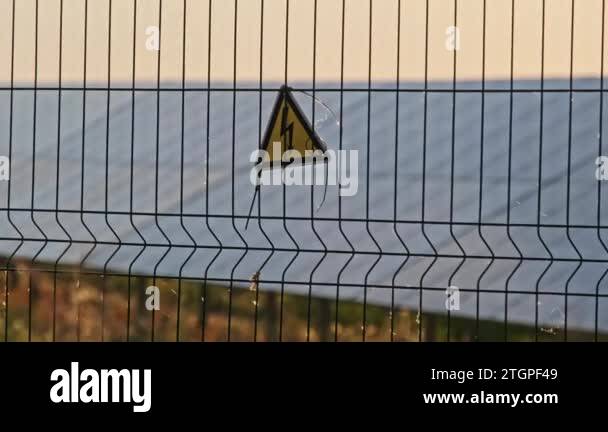 High voltage sign on a wire fence of the solar plant. Yellow triangular ...