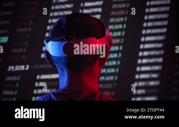 A trader in a virtual reality helmet looks at cryptocurrency charts. Young man analyzes ...