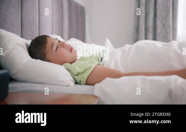 Mother caring for sick mixed race child lying in bed with flu, measuring temperature using ...