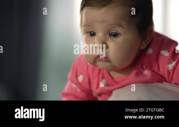 Little girl in moms arms. The baby looks into the camera and saliva ...