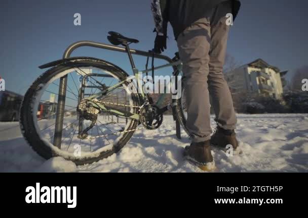 Male cyclist unlocks parked bicycle in street parking lot in snowy ...