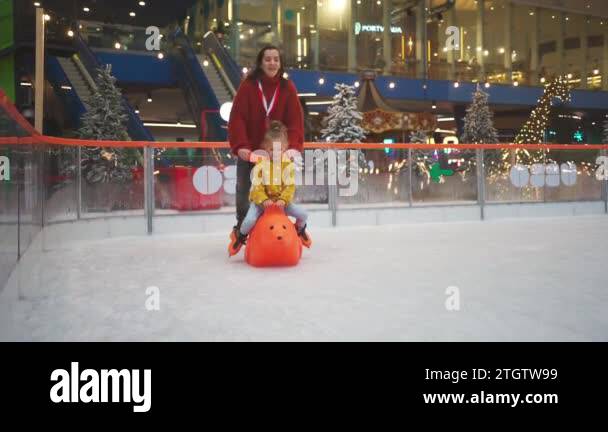 Mom with daughter have fun on ice skater rink use skating aid dolphin ...