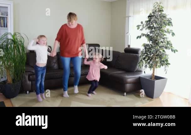 Mother nanny having fun with cute little girls dancing in living room. Happy family. Carefree ...