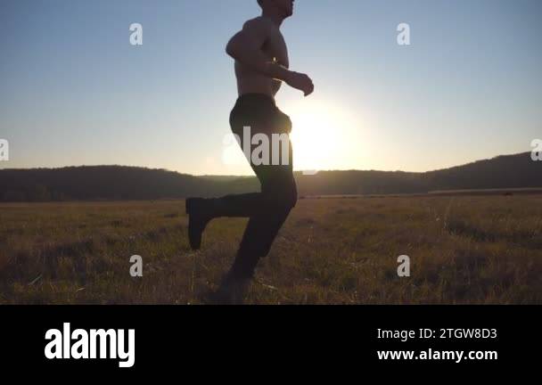 Young muscular man running through field with beautiful landscape at ...