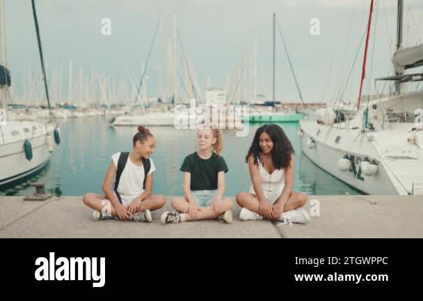 Laughing three girls friends pre-teenage sitting on the waterfront ...