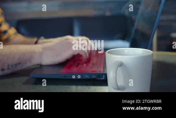 Male hands typing on keyboard of laptop at home with a cup of coffee on ...