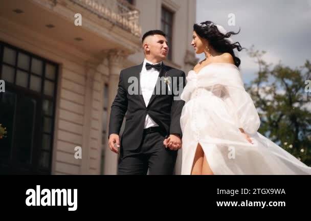 Bride and groom walking down marble stairs in luxury mansion courtyard ...