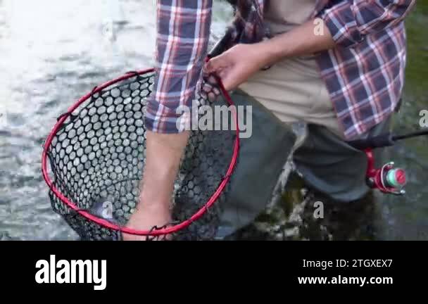 Man holds fish that was just caught in river and puts it in the fishnet ...