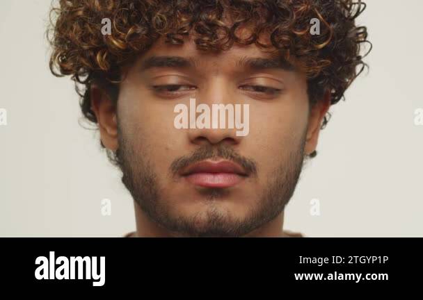Close up view of a curly young man blinking with slight smile. Cheerful ...