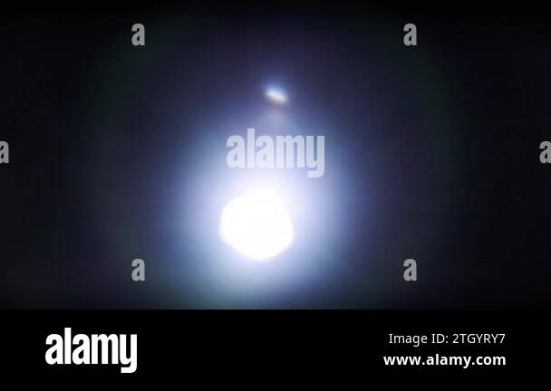 The light of a bright flashlight directed at the camera moves from side ...