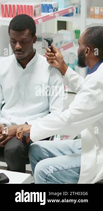 Vertical video: Health specialist consulting client with otoscope at ...