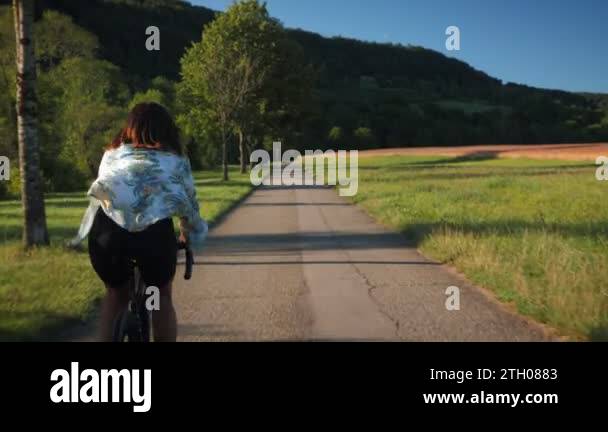 Woman in casual wear cycling on bike on cycle path along field and ...