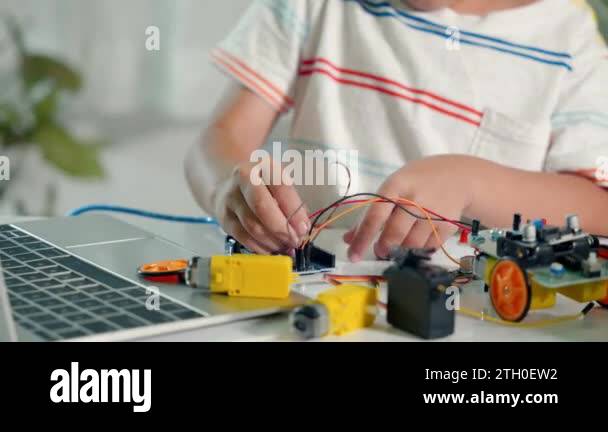 Asian kid boy plugging energy and signal cable to sensor chip with Arduino robot car, Little ...
