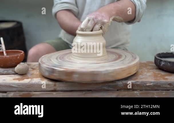 A rotating potters wheel and pottery on it, taken from the side. a man ...