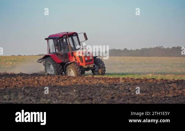 Red tractor in a field. Tractor ploughing a field with a trail of dust ...