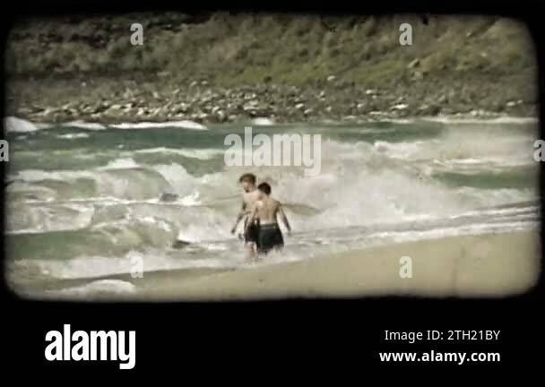 Two boys, both wearing black swimming trunks, play near strong waves on ...