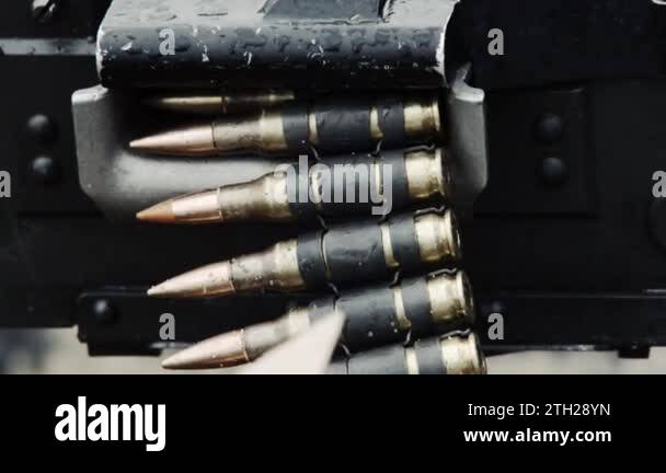 Close-up of a chain of bullets going through a belt-fed machine gun as ...