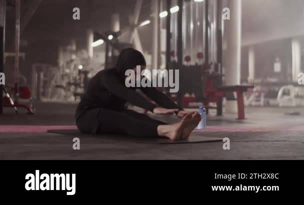Barefoot Muslim female athlete touching feet and stretching while doing ...