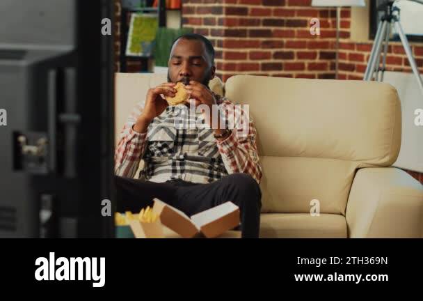 Smiling man eating hamburger with fries and beer, enjoying fast food ...