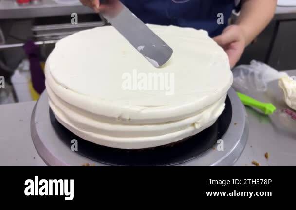 Pastry chef using spatula to frost a smooth cake with buttercream ...