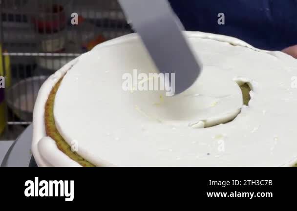 Pastry chef using spatula to frost a smooth cake with buttercream ...
