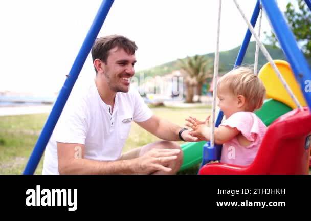 Dad swings a little girl on a swing, clapping his hands. High quality ...