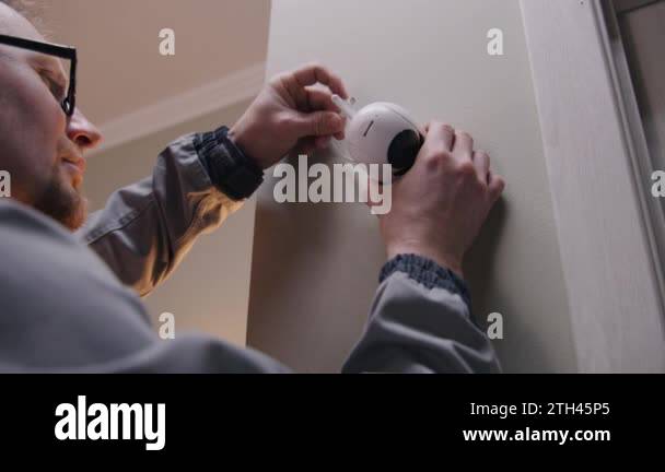 Installer in uniform puts security camera on wall mount and connects it ...