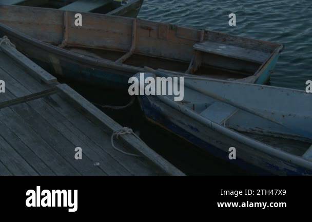 Two old, wooden rowboats with peeling paint. They are tied off to a dock and gently rocking with ...
