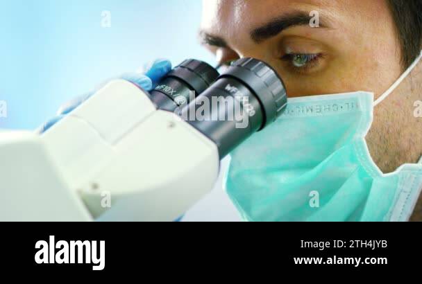 young and charming doctor look in microscope accomplishes some routine medical procedures and ...