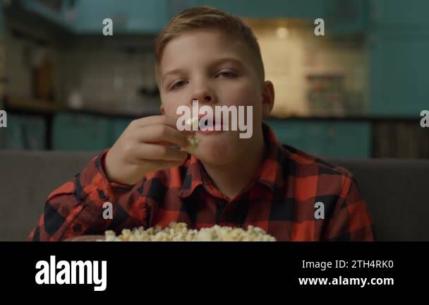 Child Eats Popcorn Looking At Camera. Boy watching TV with popcorn ...