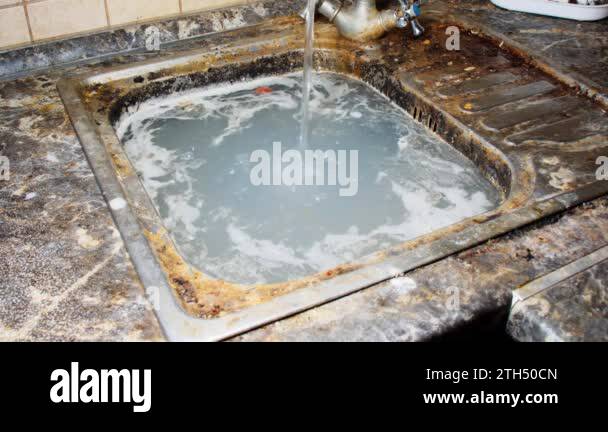 Dirty water in a dirty kitchen sink. Muddy soapy water overflows an old ...