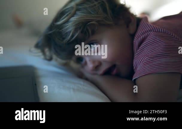 Child watching cartoons laying in bed hypnotized by screen at night ...