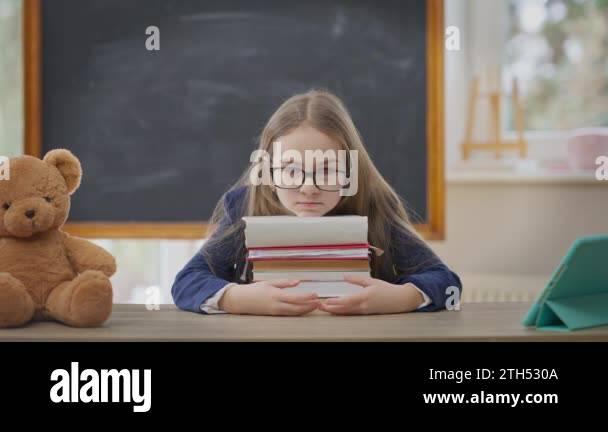 Portrait of sad teenage girl sitting in classroom with head on books ...
