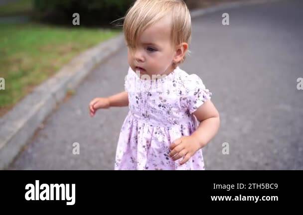 Little girl in a dress walks waving her hands along an asphalt path in ...
