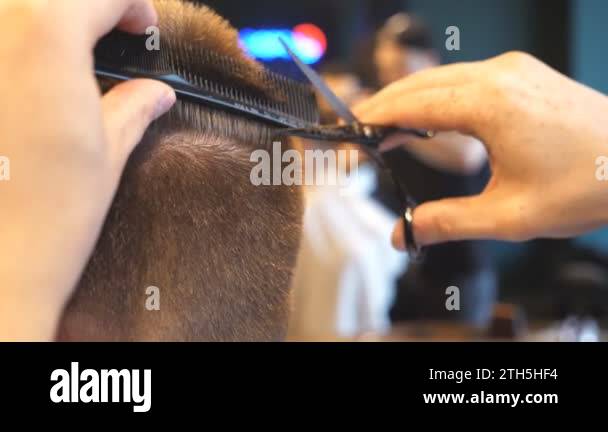 Male hands of hairdresser combing and cutting hair of customer with ...